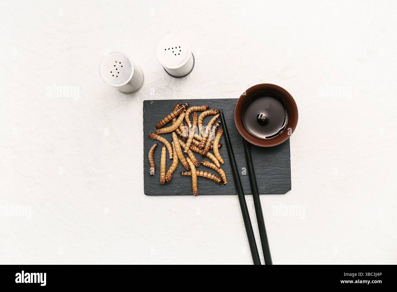 Black board with fried maggots and bowl of soy sauce on white ...