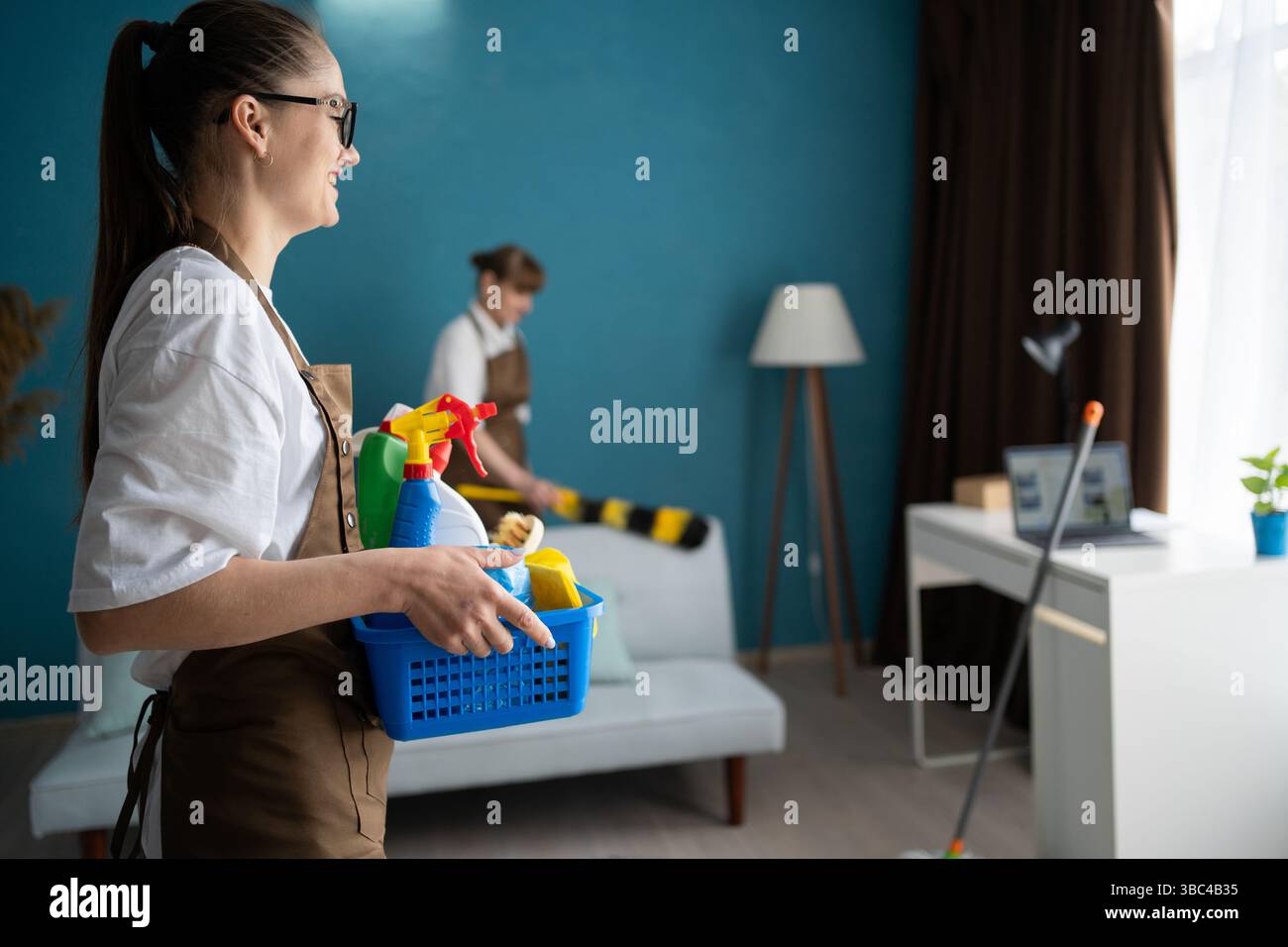 Female janitor holding basket of cleaning supplies in the living room ...