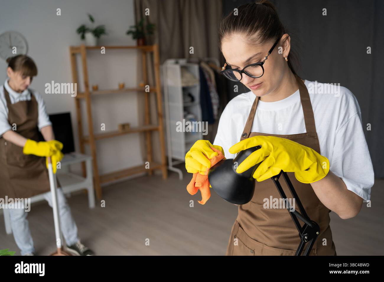 Two women cleaning home sweeping floor and wiping dust from surfaces ...