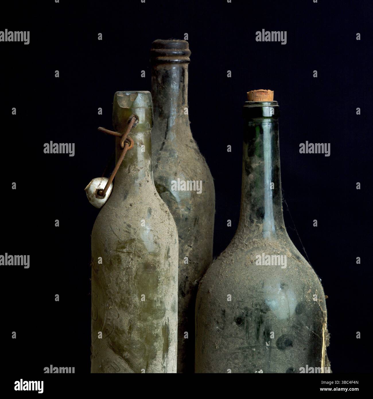 Three dusty vintage bottles stand together, covered in grime ...