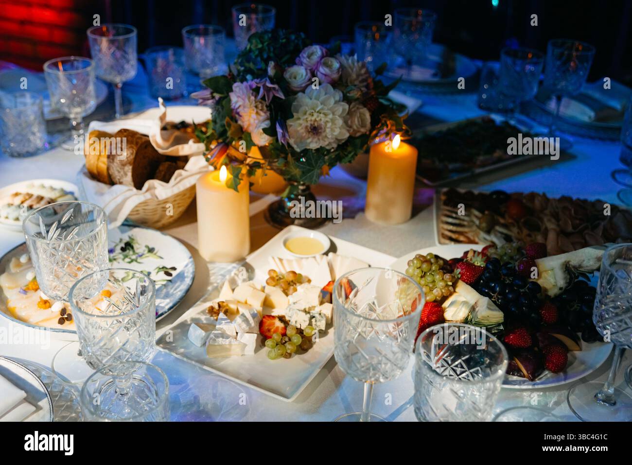 Upscale dining setup with elegant glassware, floral centerpiece, candles, assorted cheeses ...