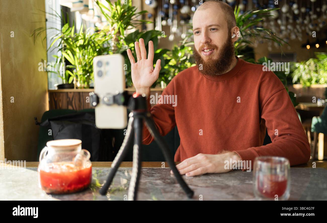 Bearded male influencer broadcasting using smartphone and tripod ...
