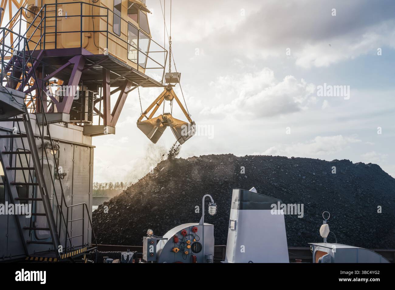 A large crane is positioned at the port, engaged in the loading of coal ...