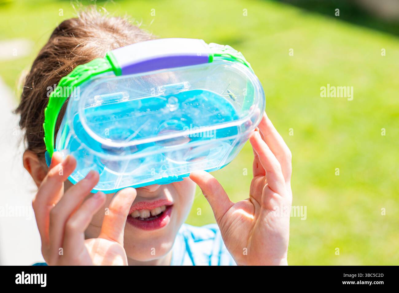 Caucasian child girl, 8 years old, observing a green grasshopper inside ...