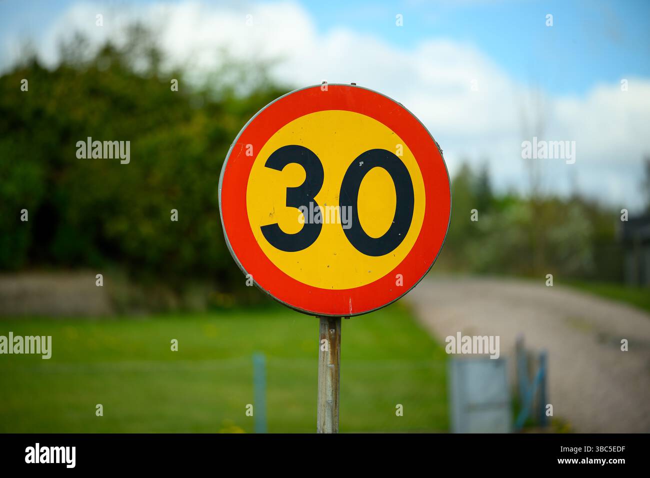 A large circular speed limit sign displays the number 30 in black on a ...
