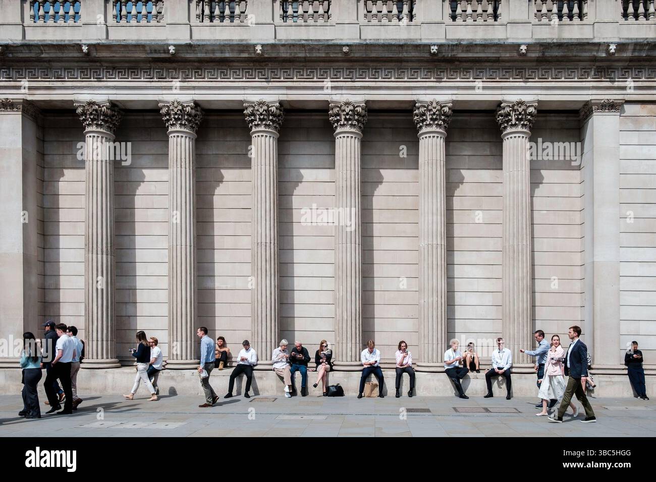 People enjoying London spring sunshine sit at base of columns of the ...