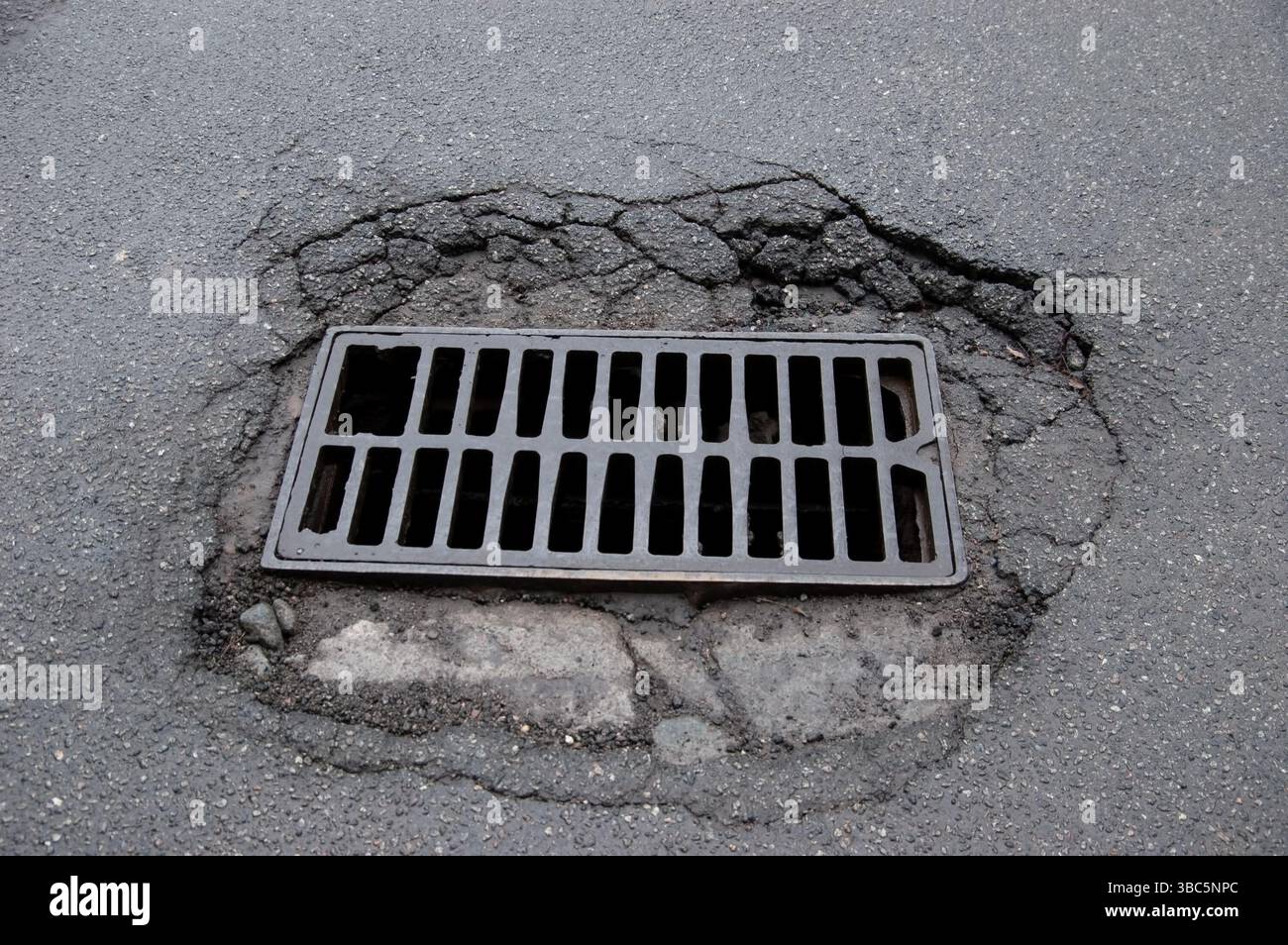 an old broken storm grate in the middle of cracked asphalt Stock Photo ...