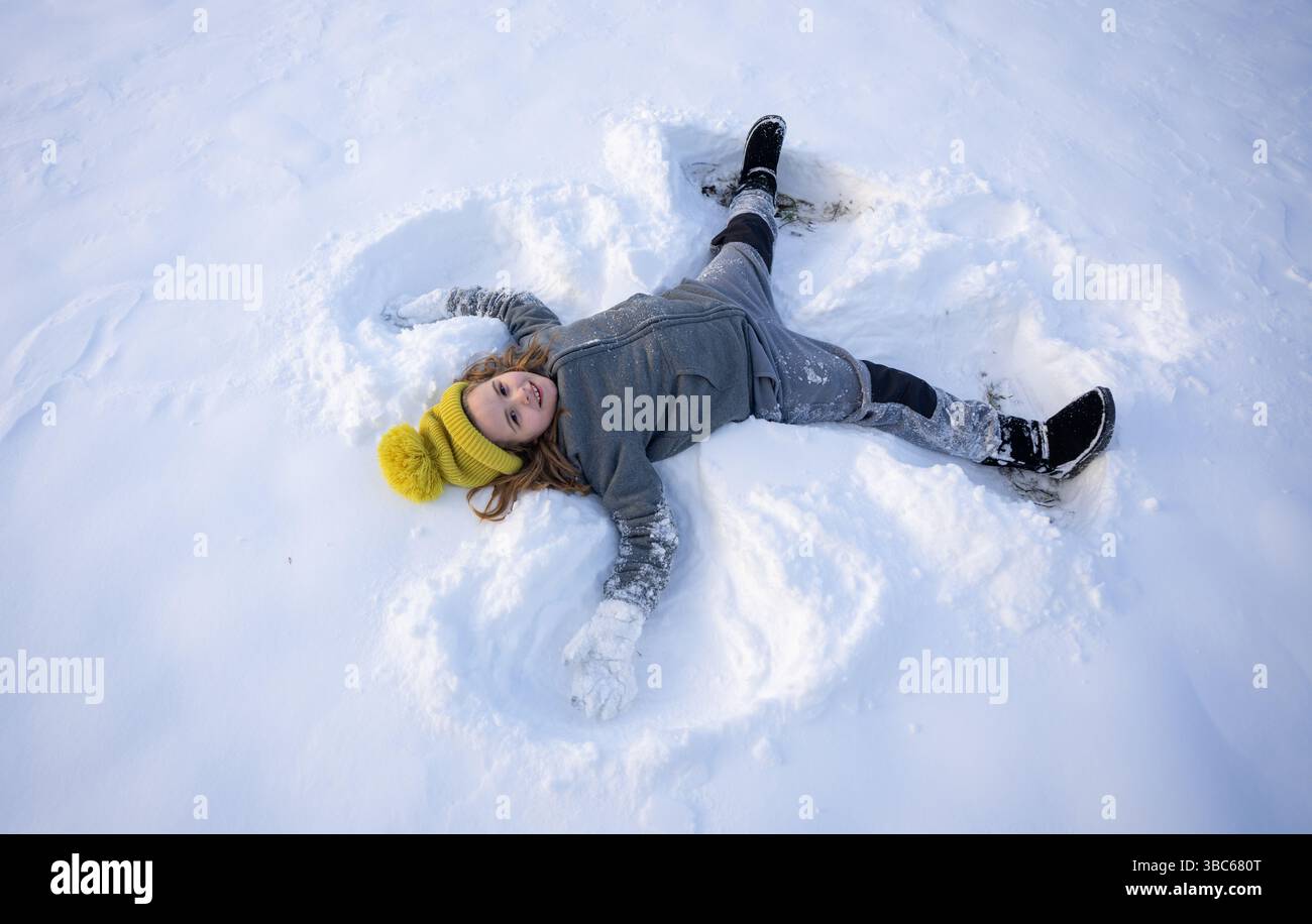 Child making a snow angel. Happy kid lying in the snow. Kid angel in ...