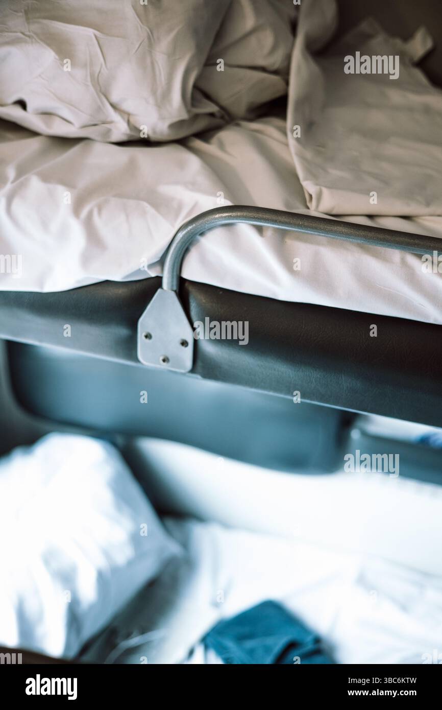 An empty train bunk bed with white sheets and a safety rail. A detail ...