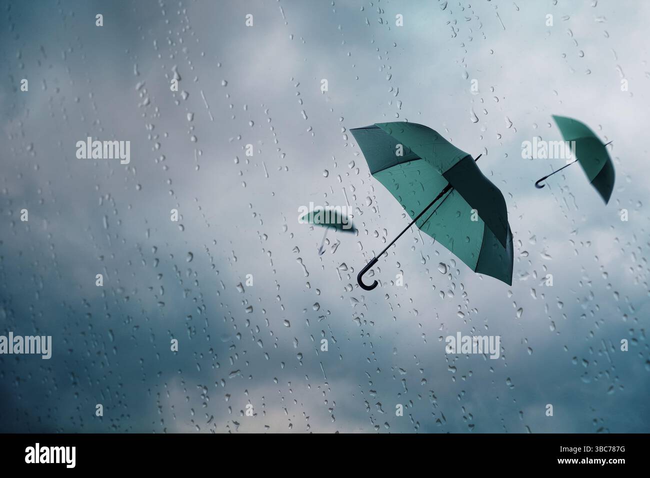 Dark green umbrellas flying in cloudy sky, view through wet window ...