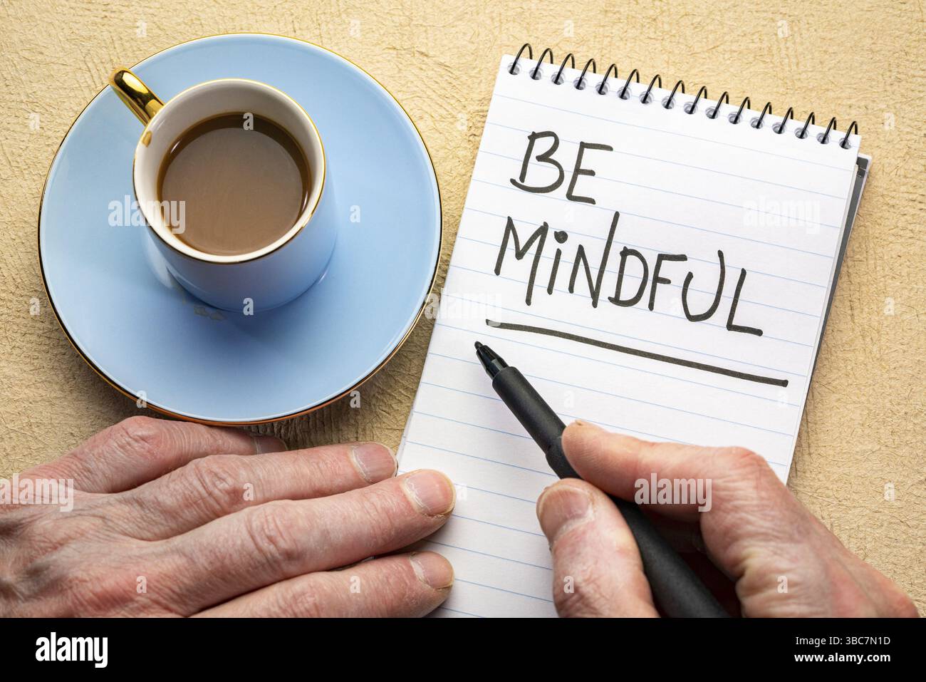 Be mindful - man hand writing a note with a black marker in a spiral ...