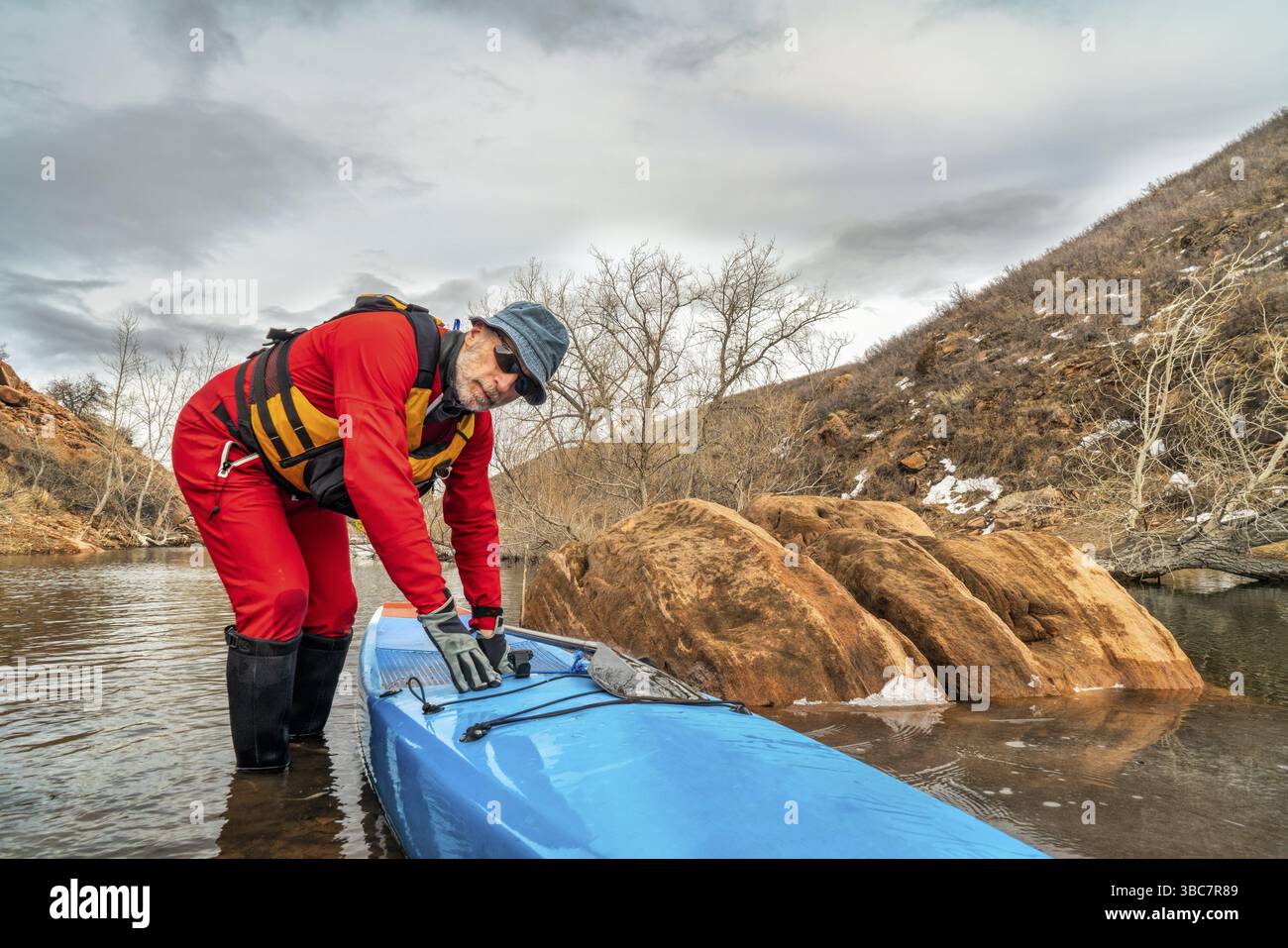 Senior male paddler in a dry suit and life jacket is launching his ...