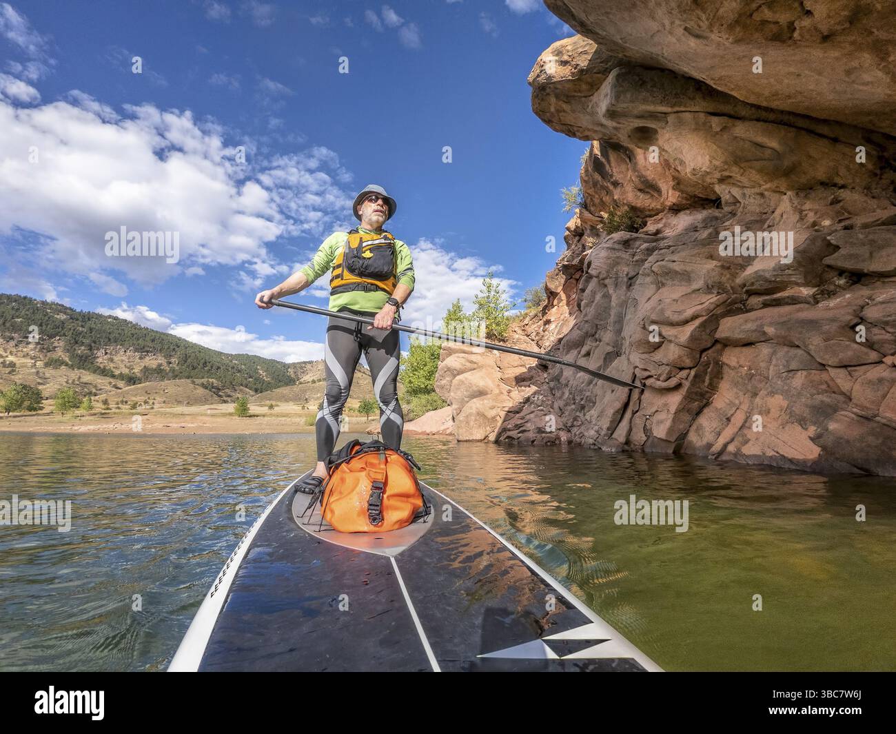 Senior man paddling a stand up paddleboard a mountain lake with ...