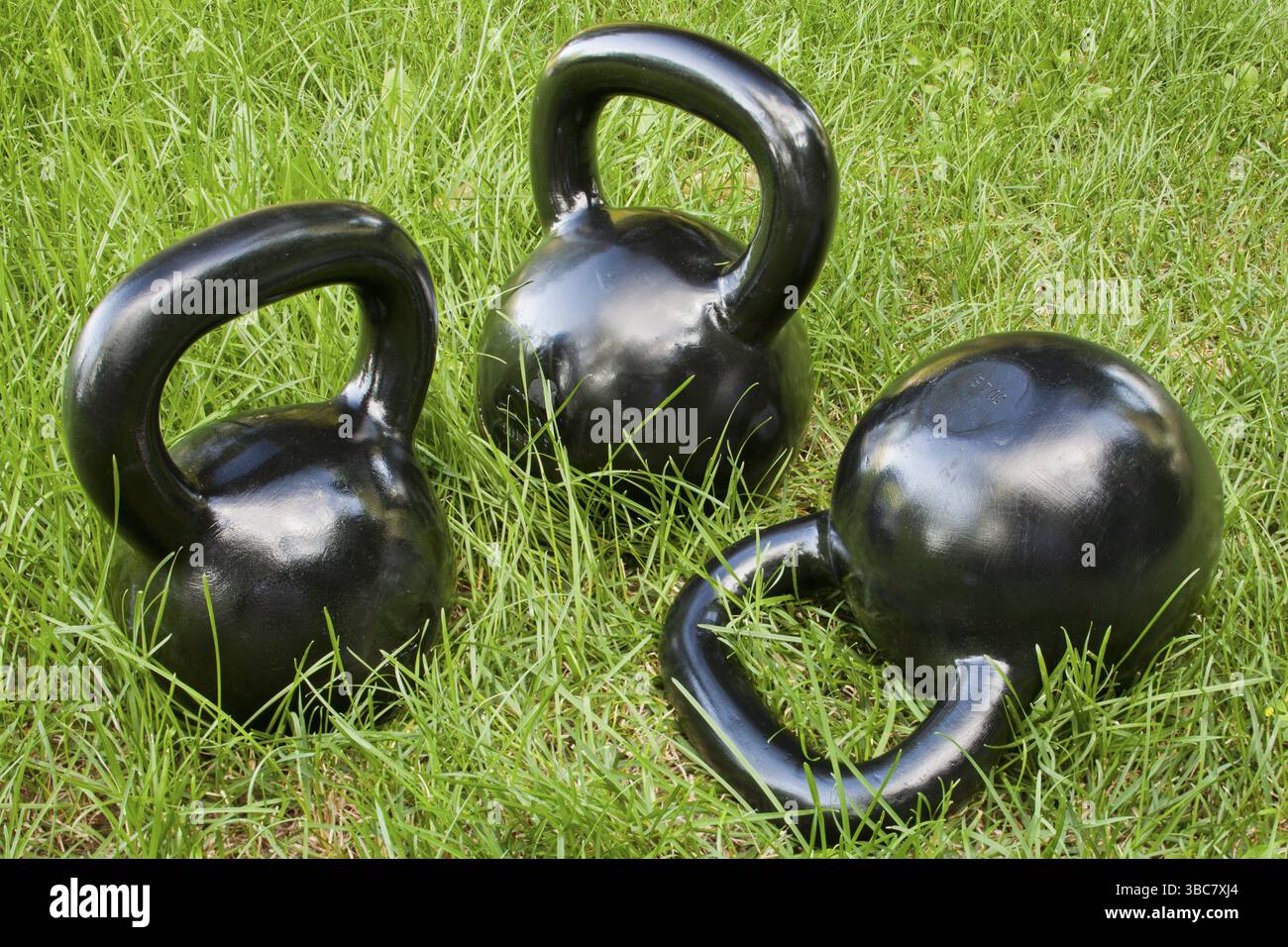 Three heavy iron kettlebells in green grass - outdoor fitness concept ...
