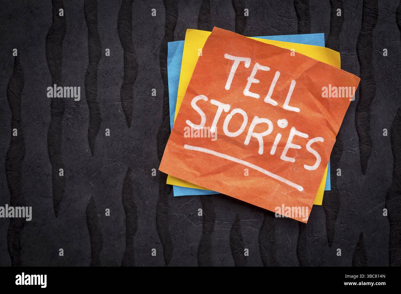 Tell stories reminder note - handwriting on a sticky note against black ...