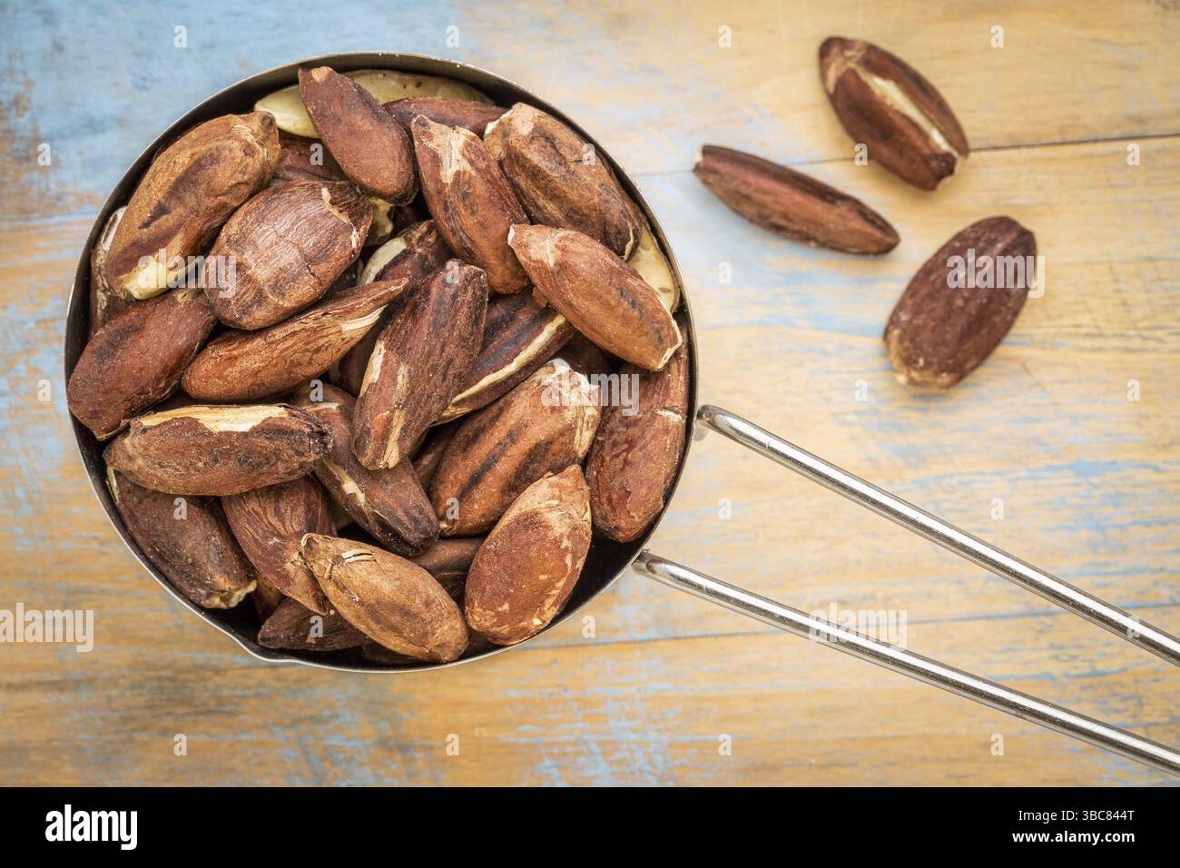Metal measuring scoop of roasted pili nuts against wood background ...
