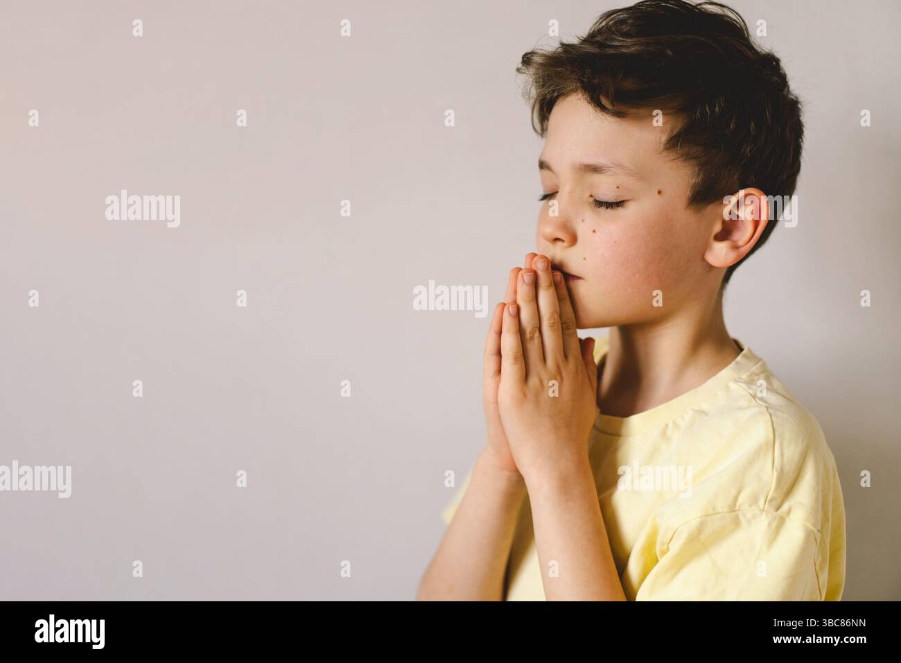 A boy with folded hands in front of him, he prays in his room Stock ...