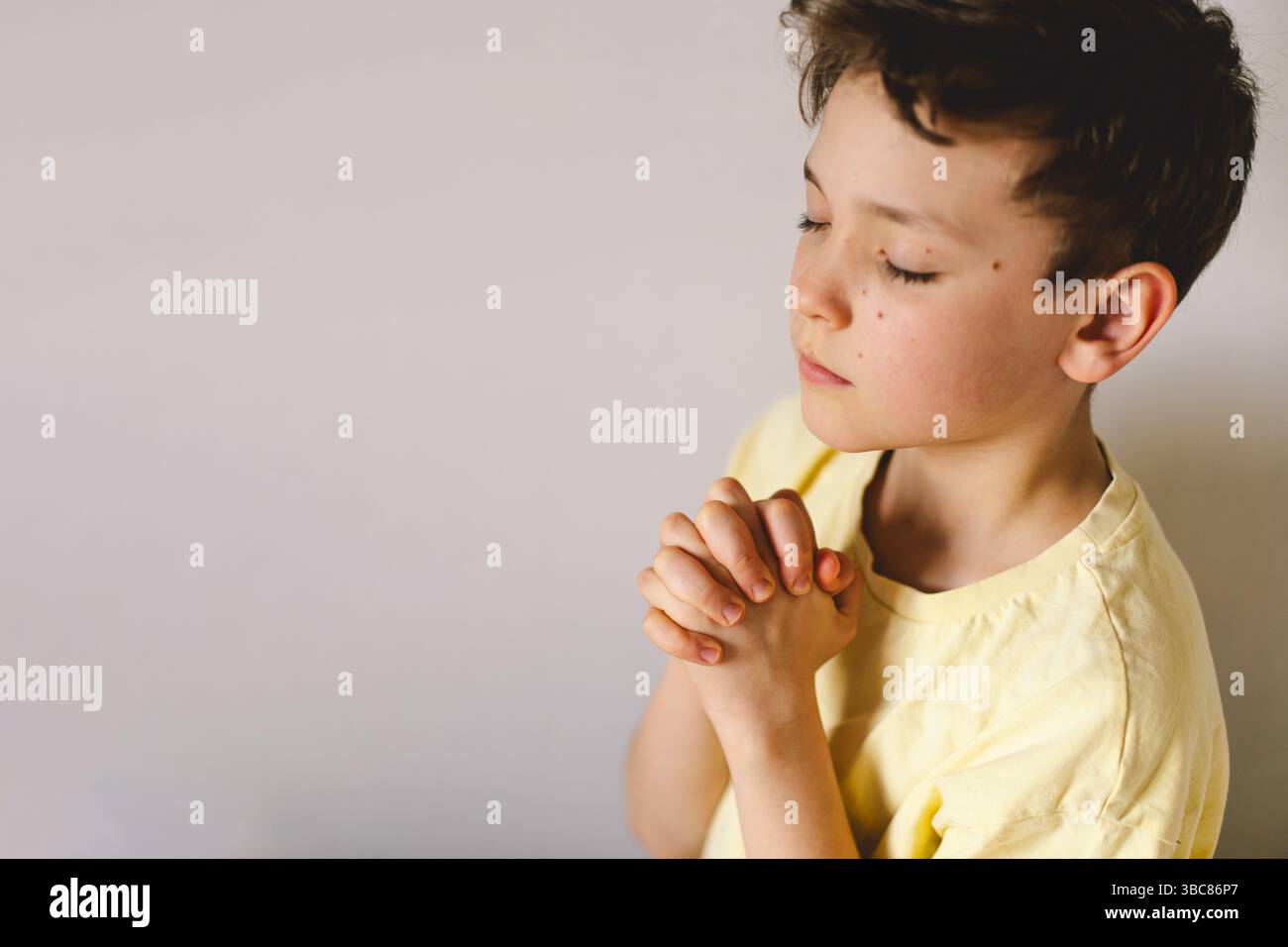 A boy with folded hands in front of him, he prays in his room Stock ...