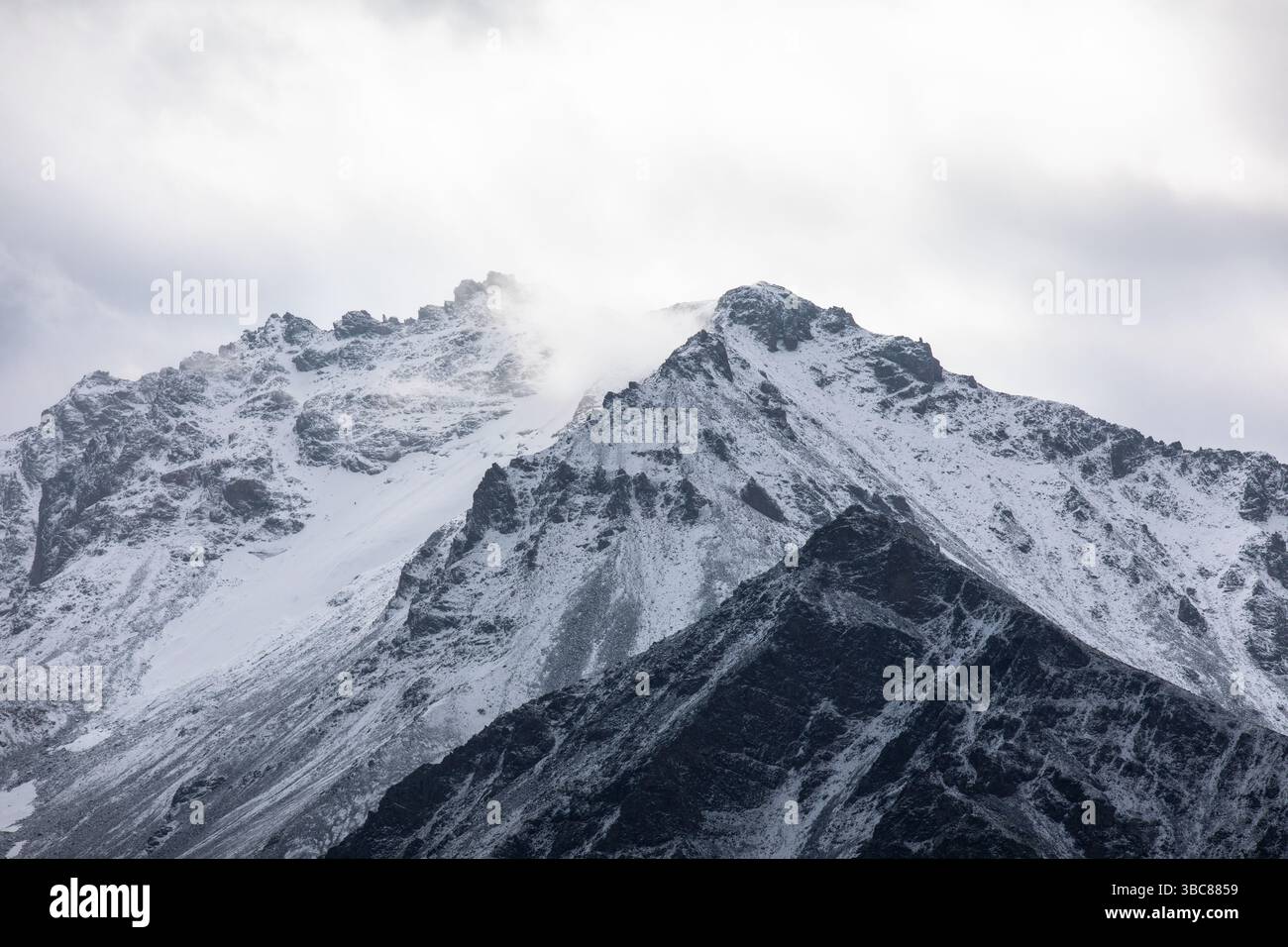 Snow-covered rugged mountain peak under cloudy sky Stock Photo - Alamy