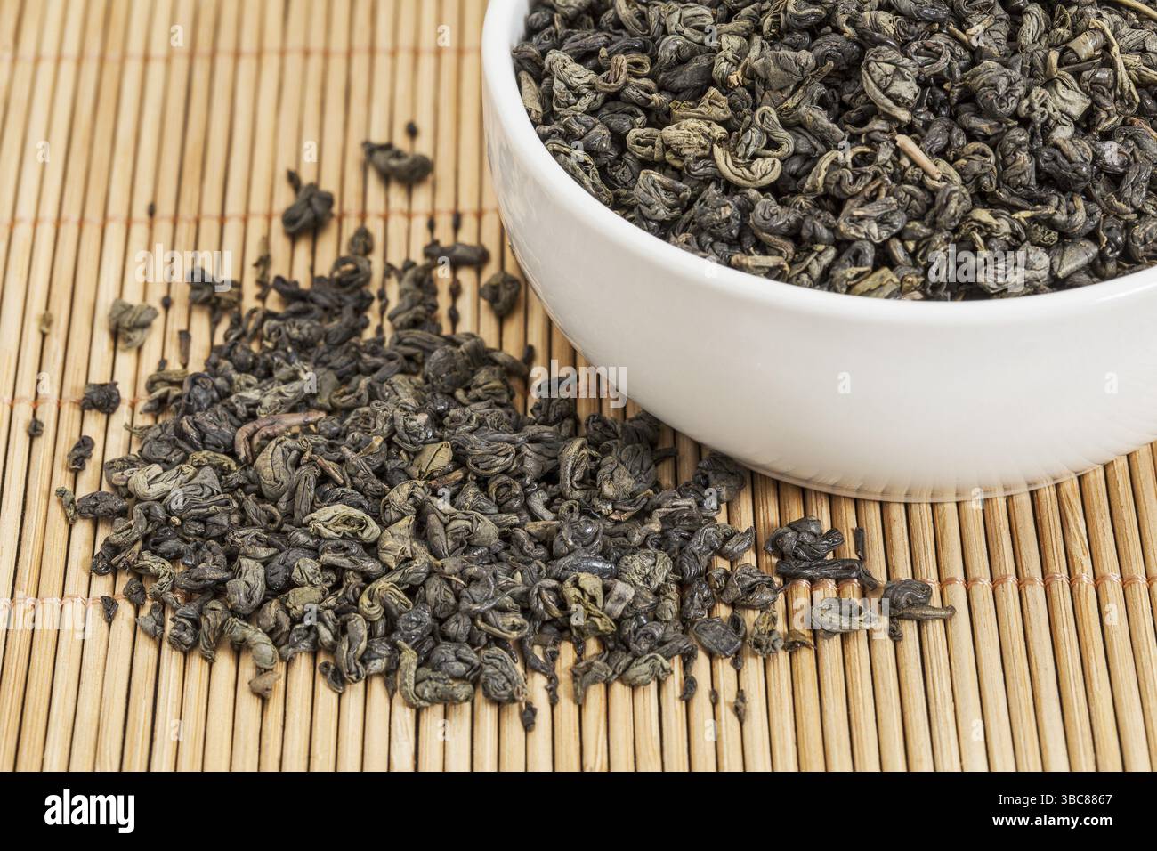 Loose leaf gunpowder green tea in a white china cup and spilled over ...