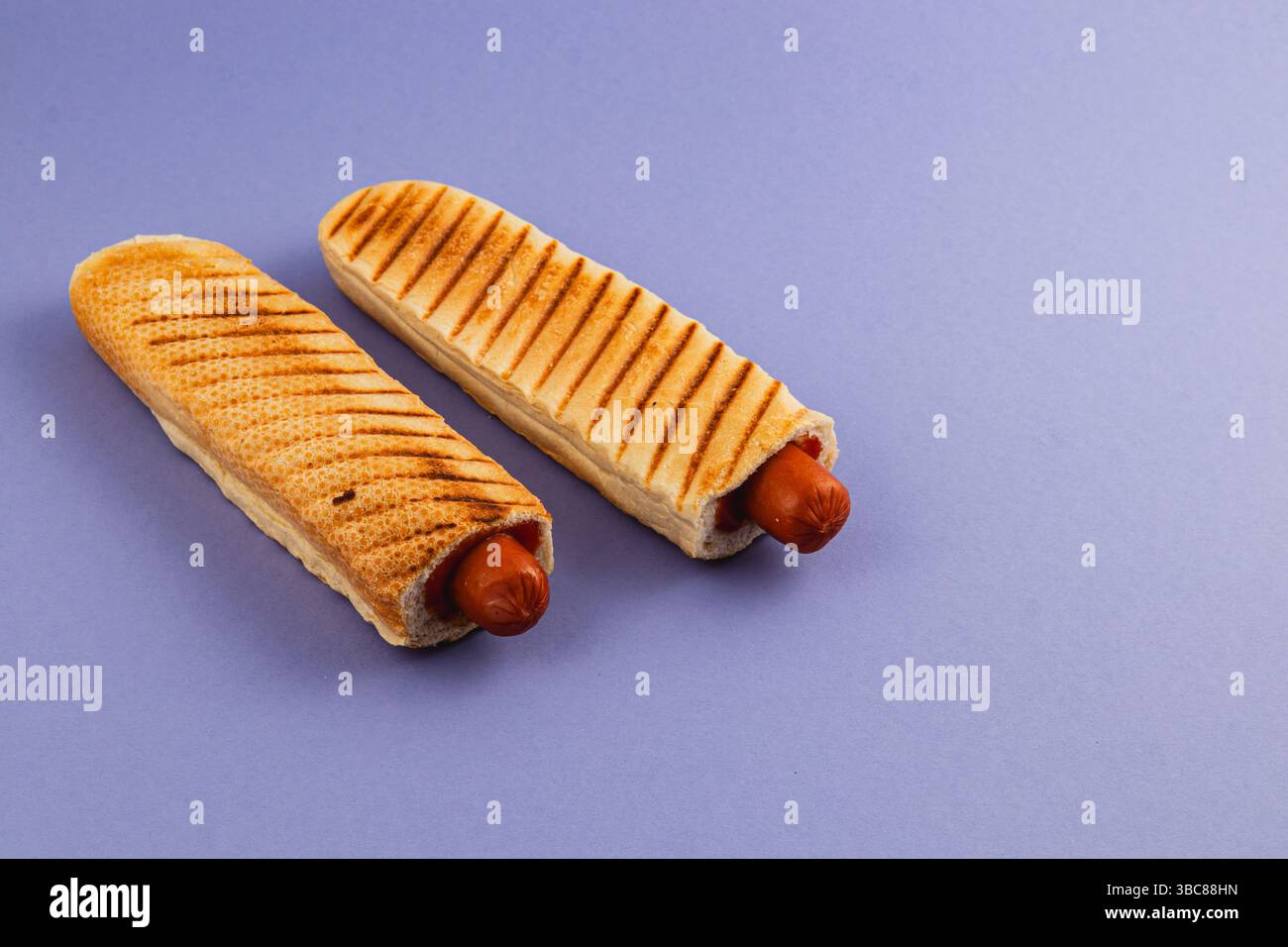 Two grilled hot dogs nestled in toasted bread rolls are placed on a ...