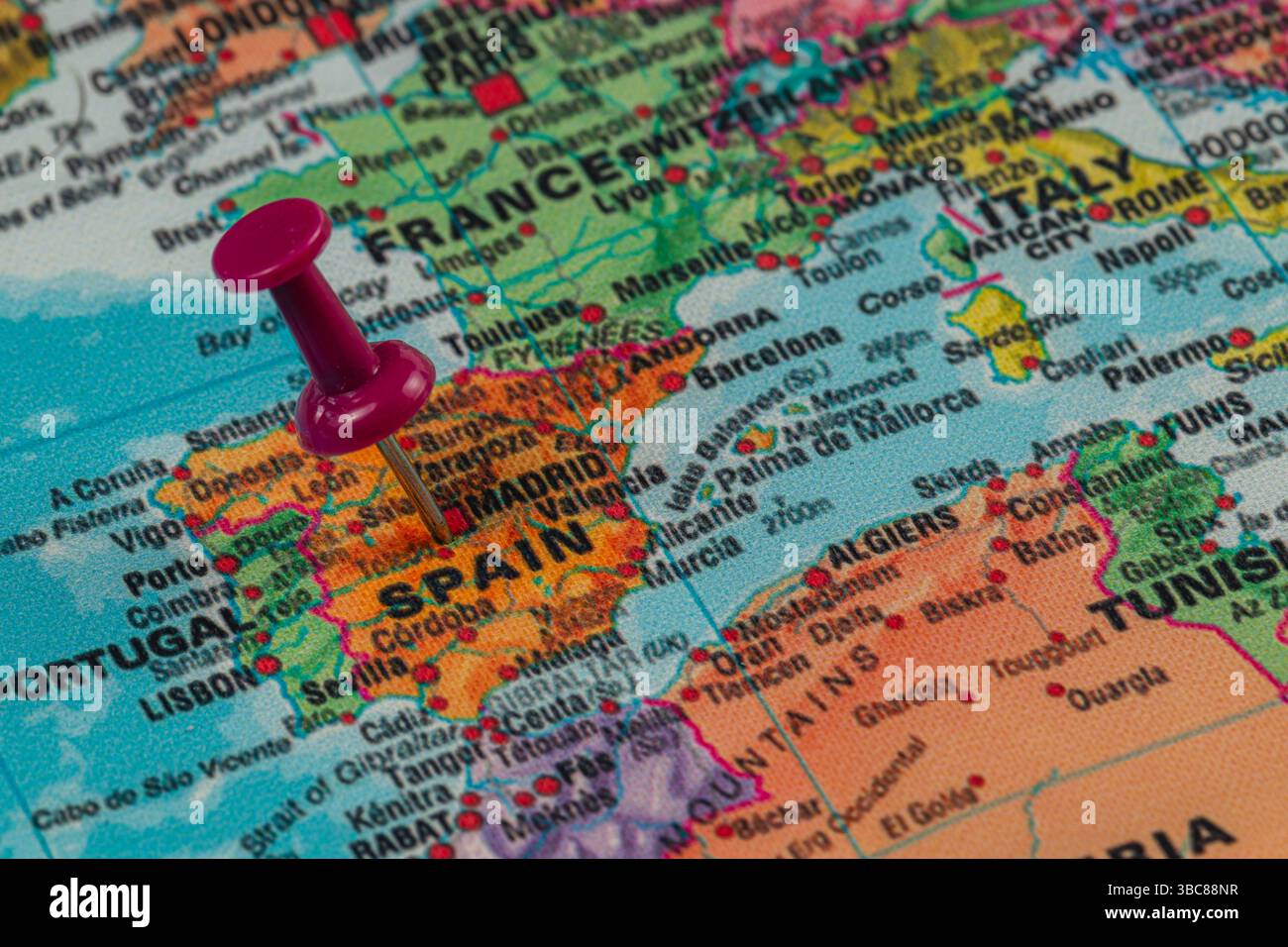 A bright pushpin marks the location of Spain on a colorful map of ...