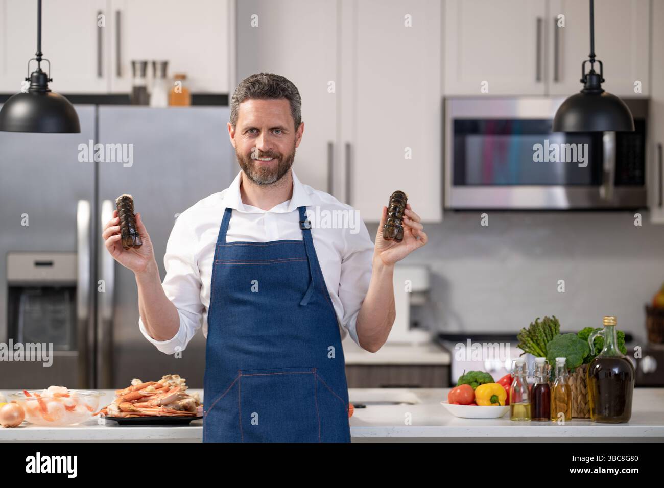 Hispanic man in kitchen with sea food. Mature man cook lobster tail ...