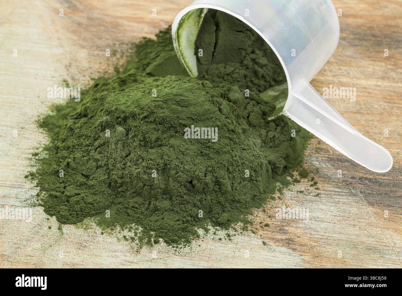 Hawaiian spirulina powder spilling of a plastic measuring scoop, wooden ...