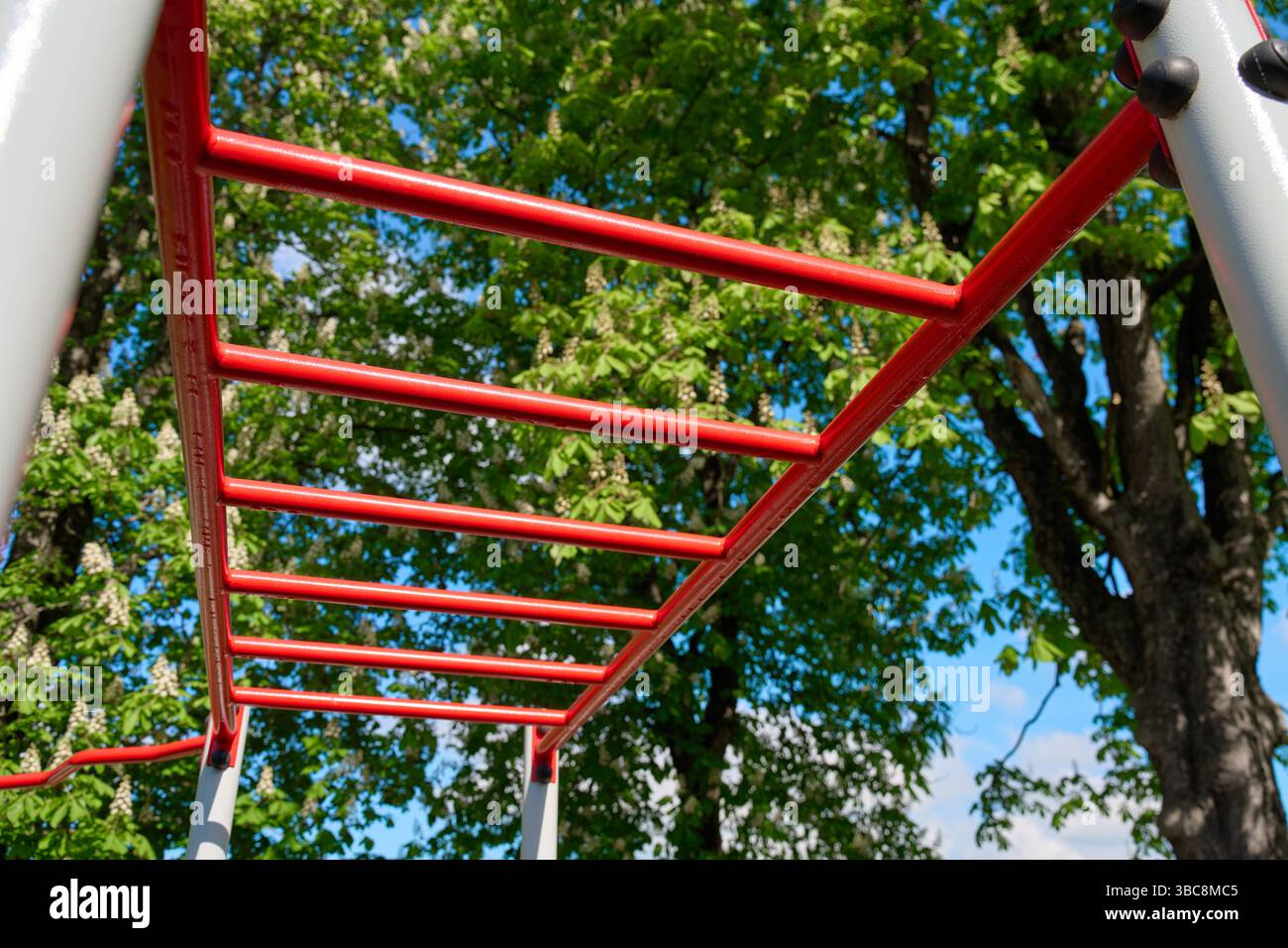 Red outdoor monkey bars in park with green trees. Fitness playground ...