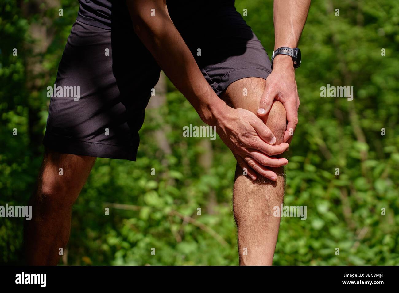 Runner holding knee in pain during workout in summer park. Man has ...