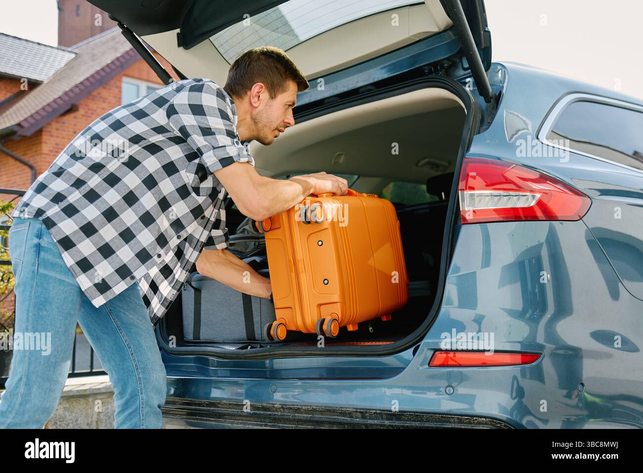 Man preparing for journey, loading suitcase in car trunk. Male traveler ...