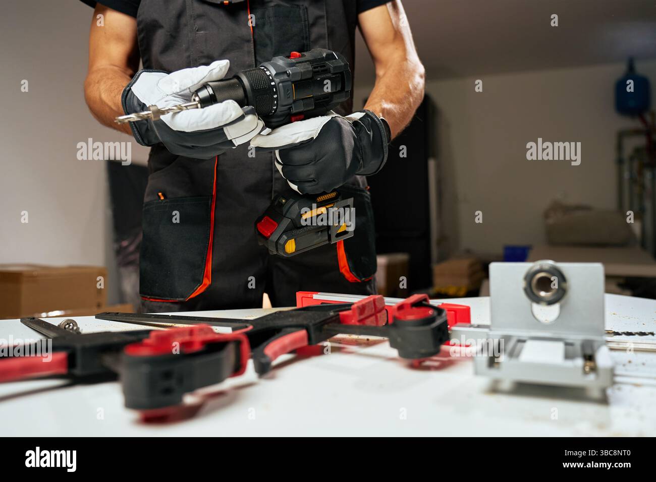 Person wearing safety gloves and work overalls holding cordless power ...