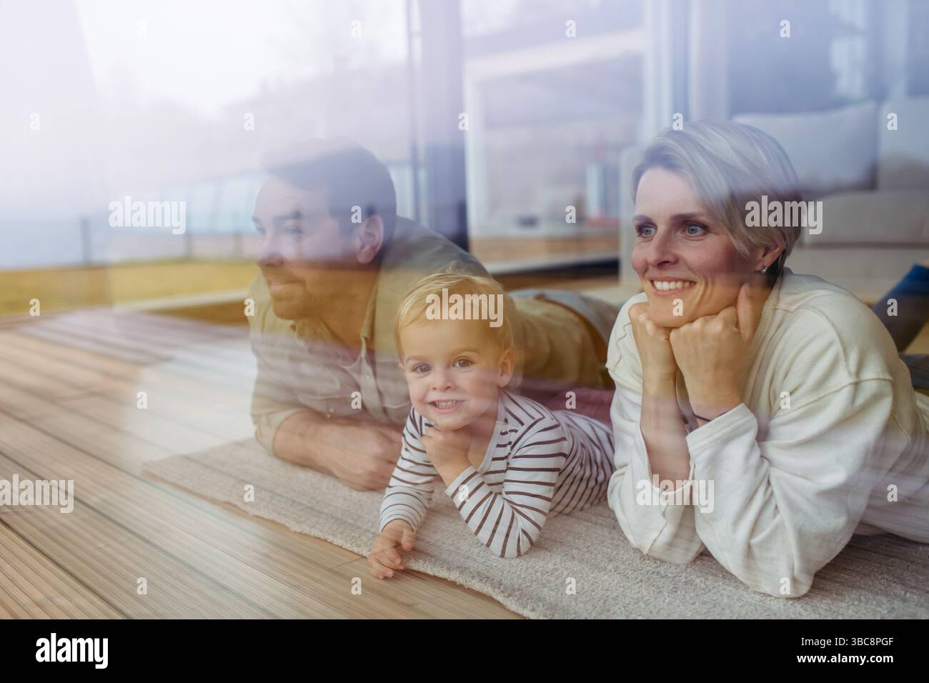 Parents looking out of window with little son, lying on floor Stock ...