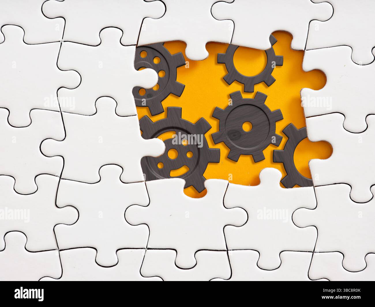Interlocking gears are partially revealed beneath a white jigsaw puzzle ...