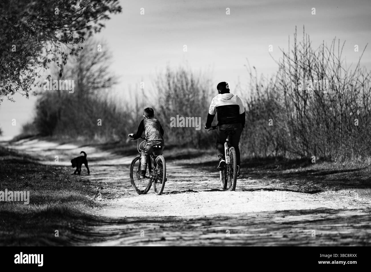 A black and white photo of two figures on bicycles traversing a dirt ...