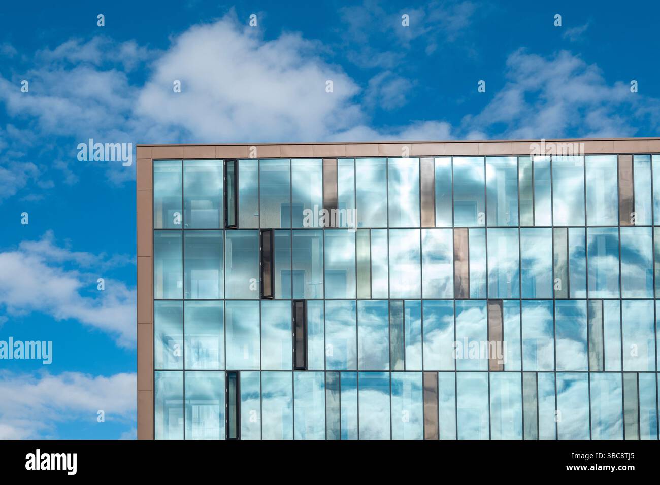 Modern minimalist glass building with blue and scattered white clouds ...