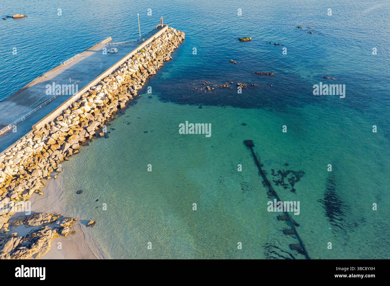 aerial view of a jetty extending into clear ocean water at sunset ...