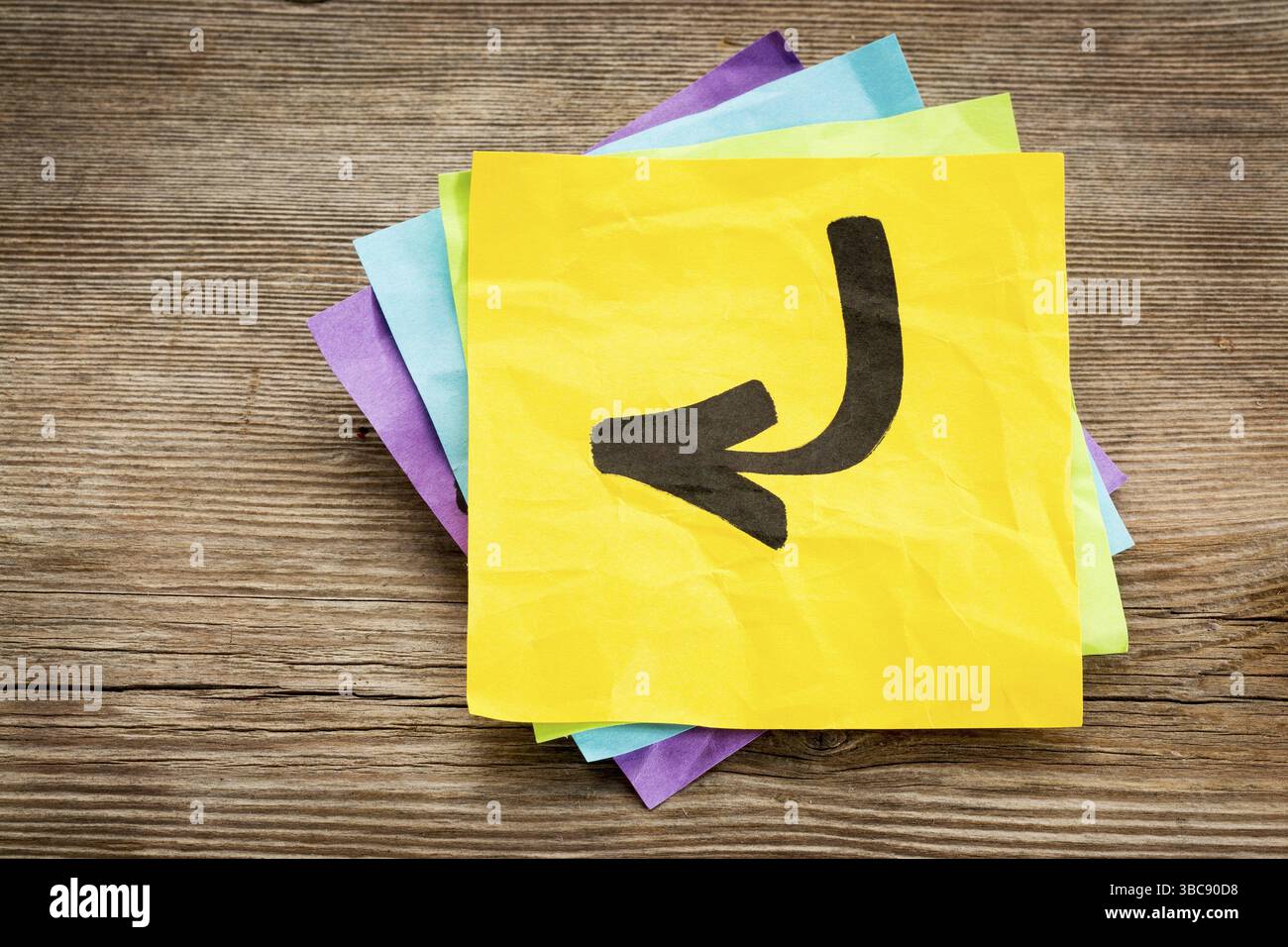 Black arrow on a yellow sticky note against grained wood Stock Photo ...
