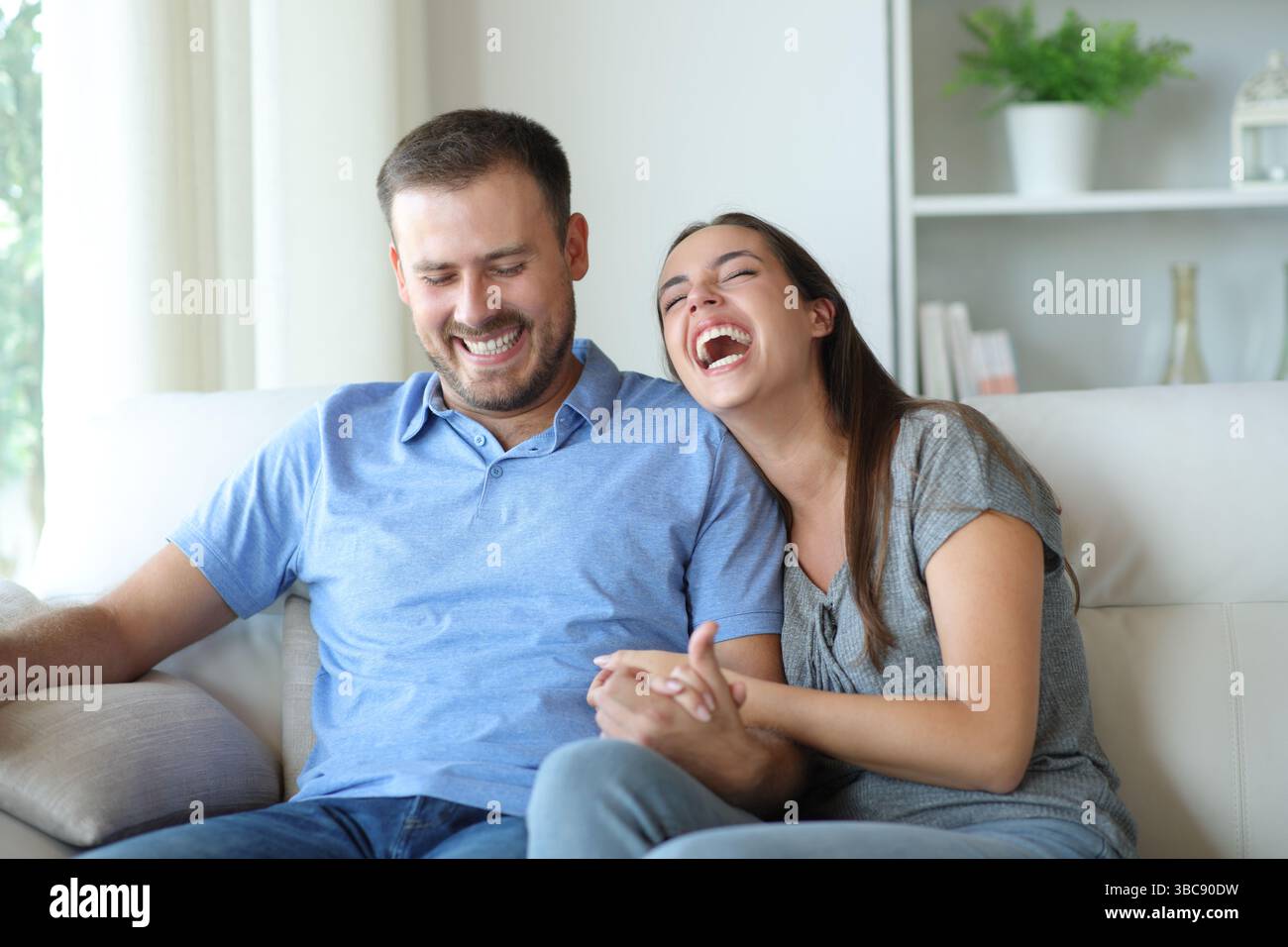 Couple at home laughing hilariously sitting on a couch Stock Photo - Alamy