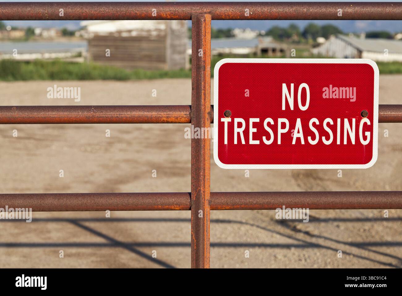 Red no trespassing sign on an iron gate with out of focus farm building ...
