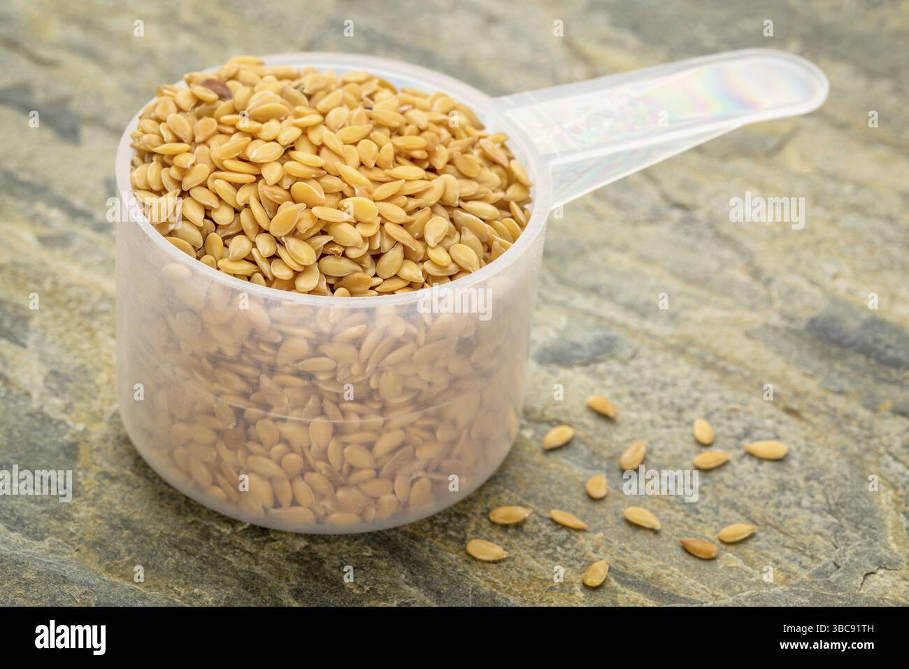 Gold flax seeds in a measuring scoop against slate rock background ...