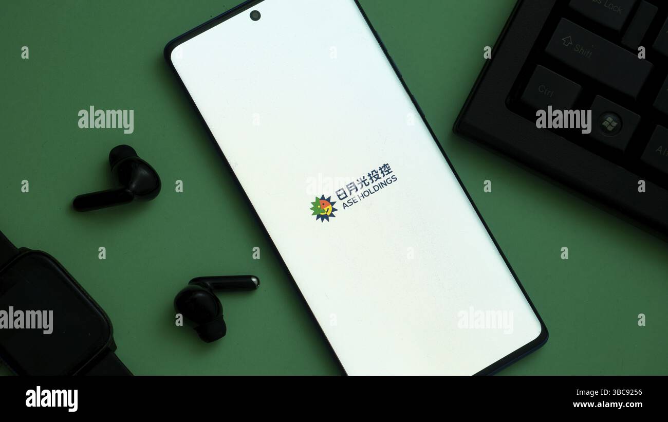 Smartphone showing ASE Holdings logo on white screen, with earphones on ...