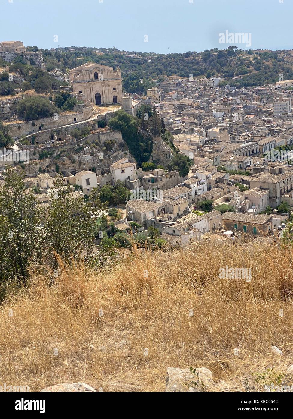 Scicli's historic stone buildings rising above dry golden grasslands ...
