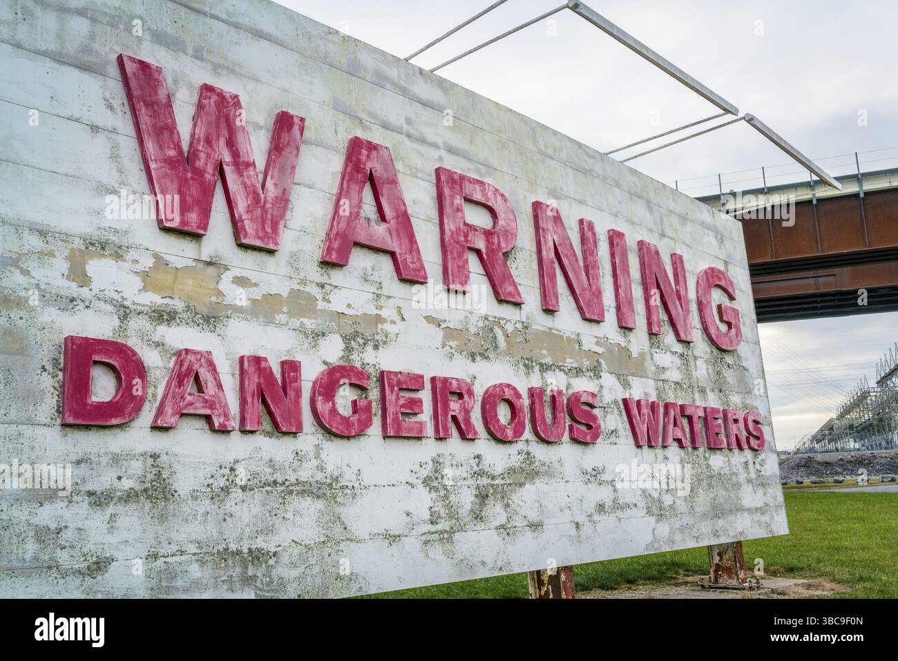Warning dangerous waters - a big grunge sign below a river dam and ...