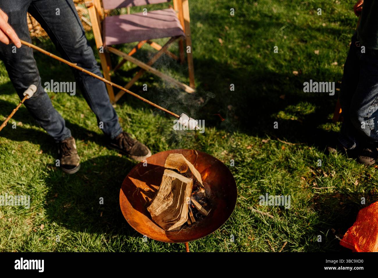 Person roasting marshmallow over a backyard fire pit in sunlight Stock ...