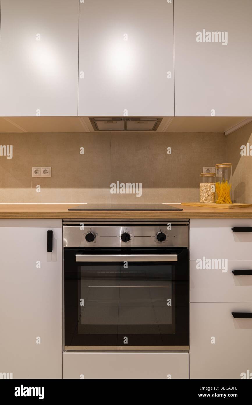 Front view of a modern kitchen cooktop and oven with white cabinets and ...