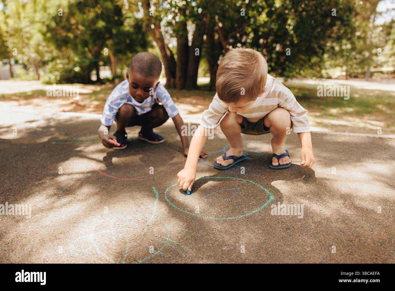 Two kids drawing colorful chalk art on a sunny day in a park ...