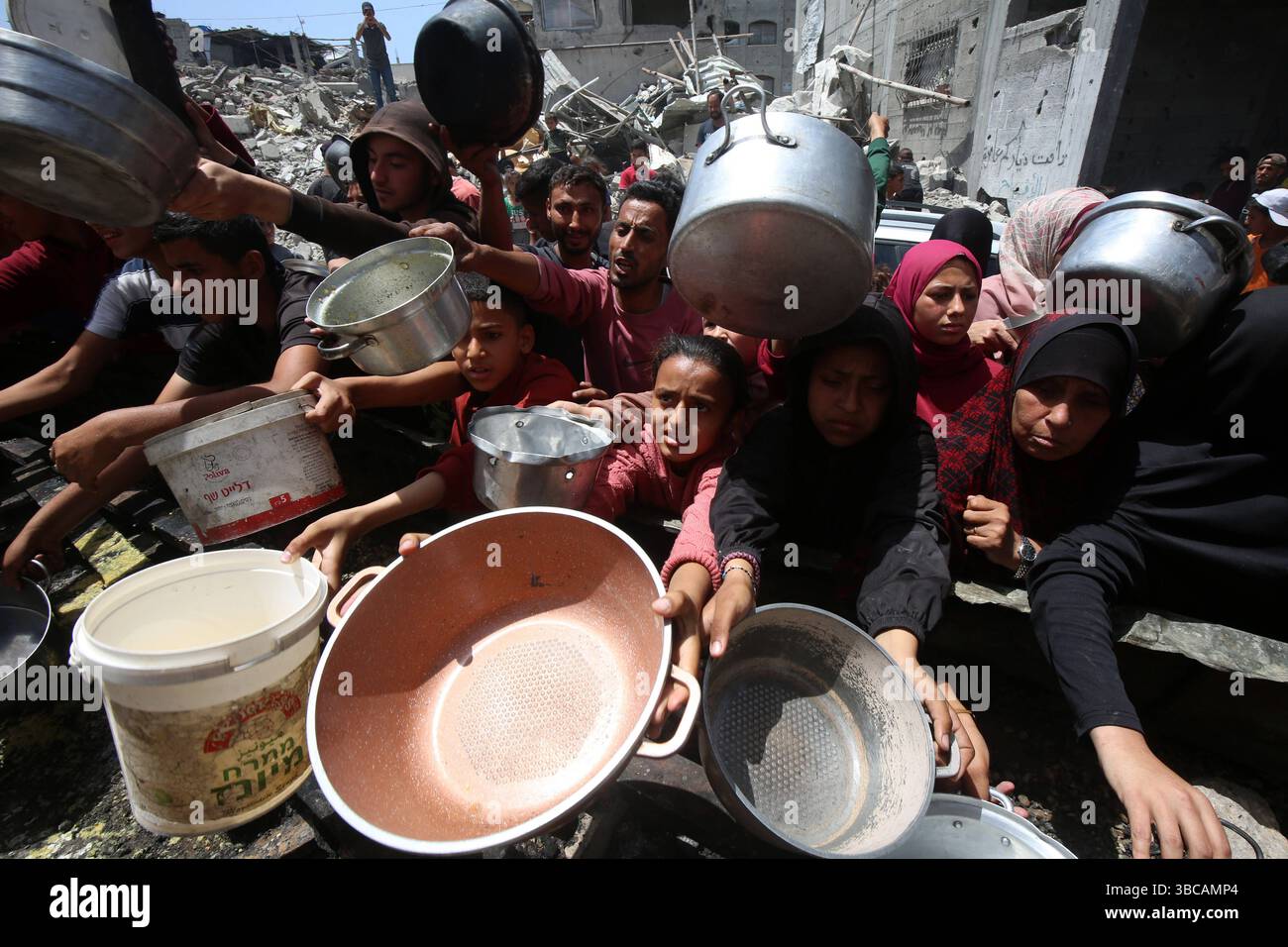 Palestinians wait in long queues to receive pots of food distributed by ...