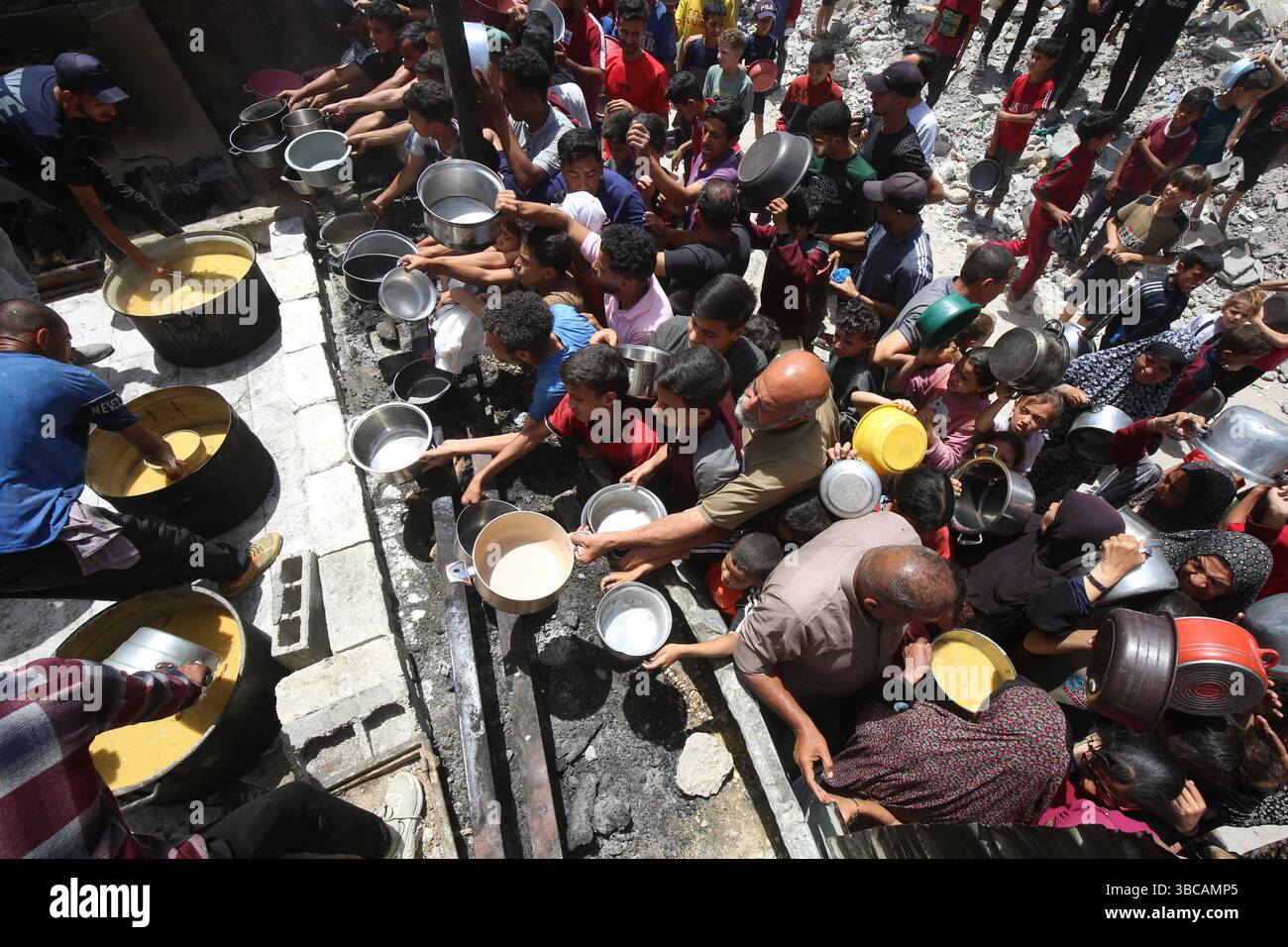 Palestinians wait in long queues to receive pots of food distributed by ...