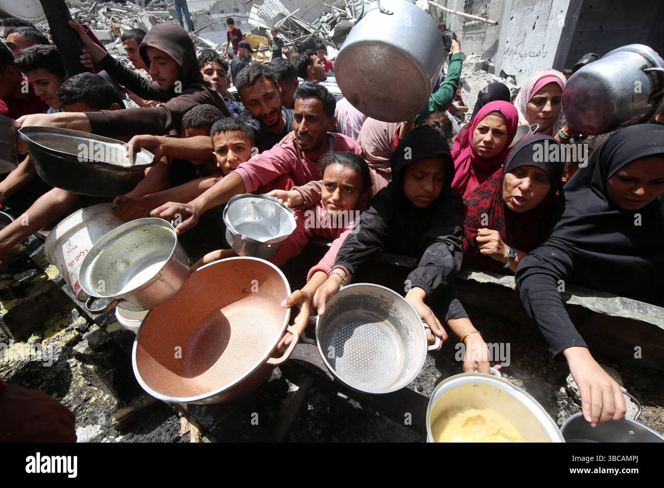 Palestinians wait in long queues to receive pots of food distributed by ...